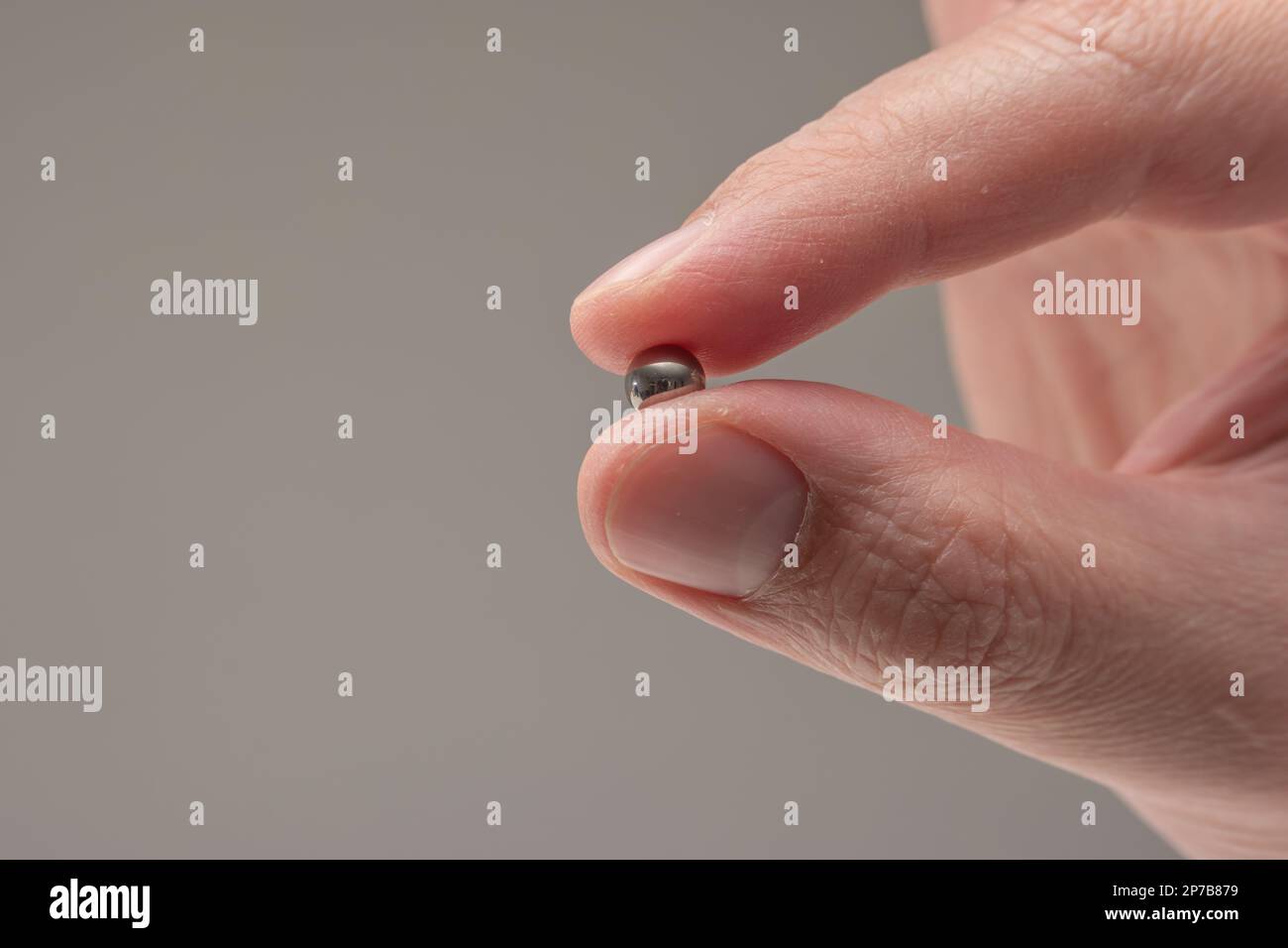 Very small metal bearing ball held between fingers by Caucasian male ...