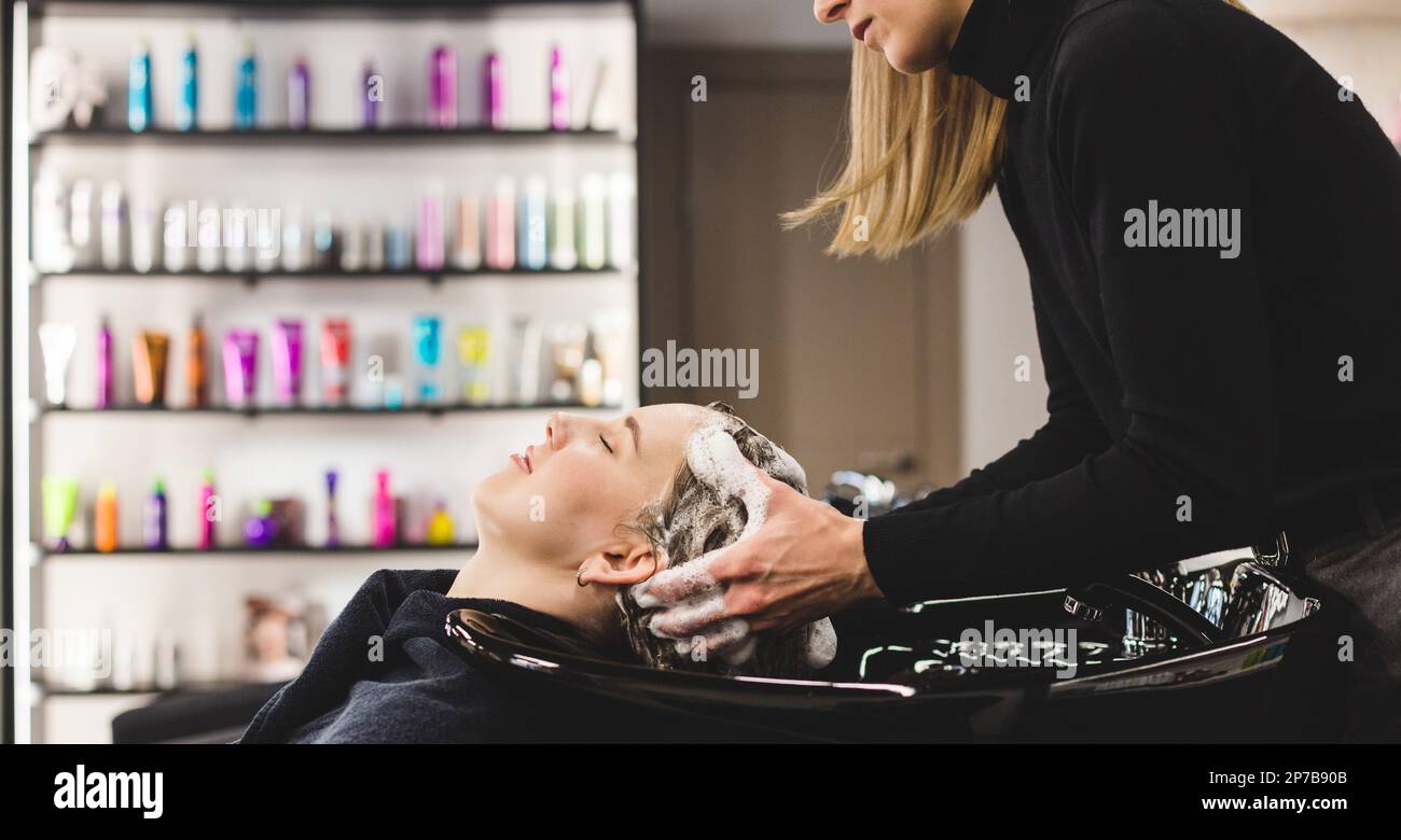 Master woman hairdresser washes hair of a girl with shampoo before ...