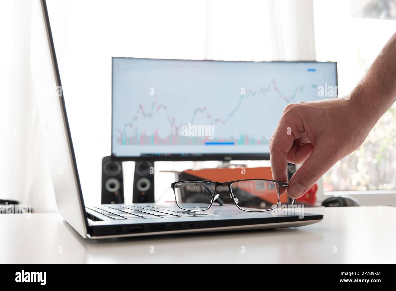 Clear reading glasses, black rim, on a laptop keypad. Blurred large computer monitor in the ...