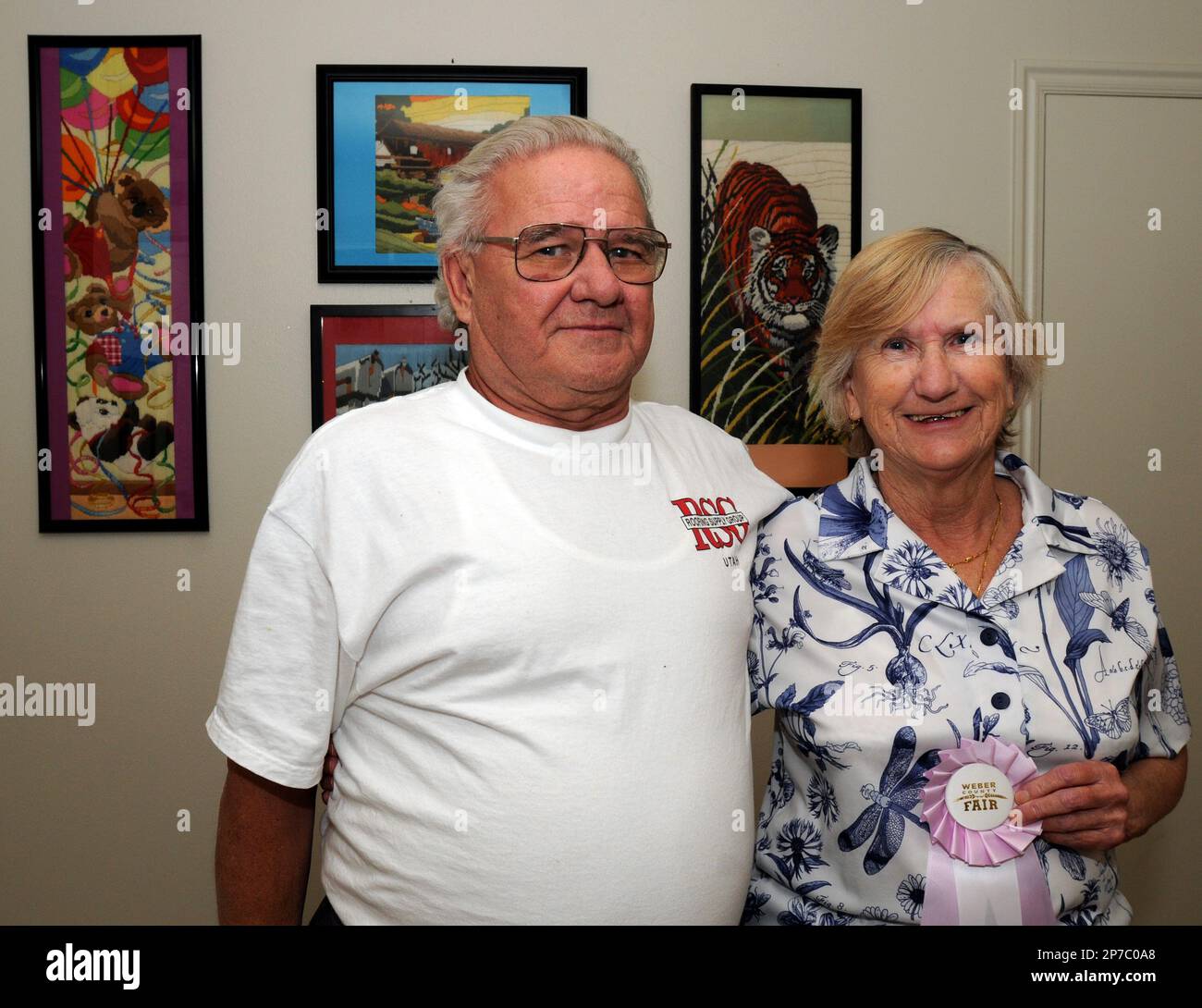 Archie and Irene Kelly stand in front of a few longstitch pieces of art ...