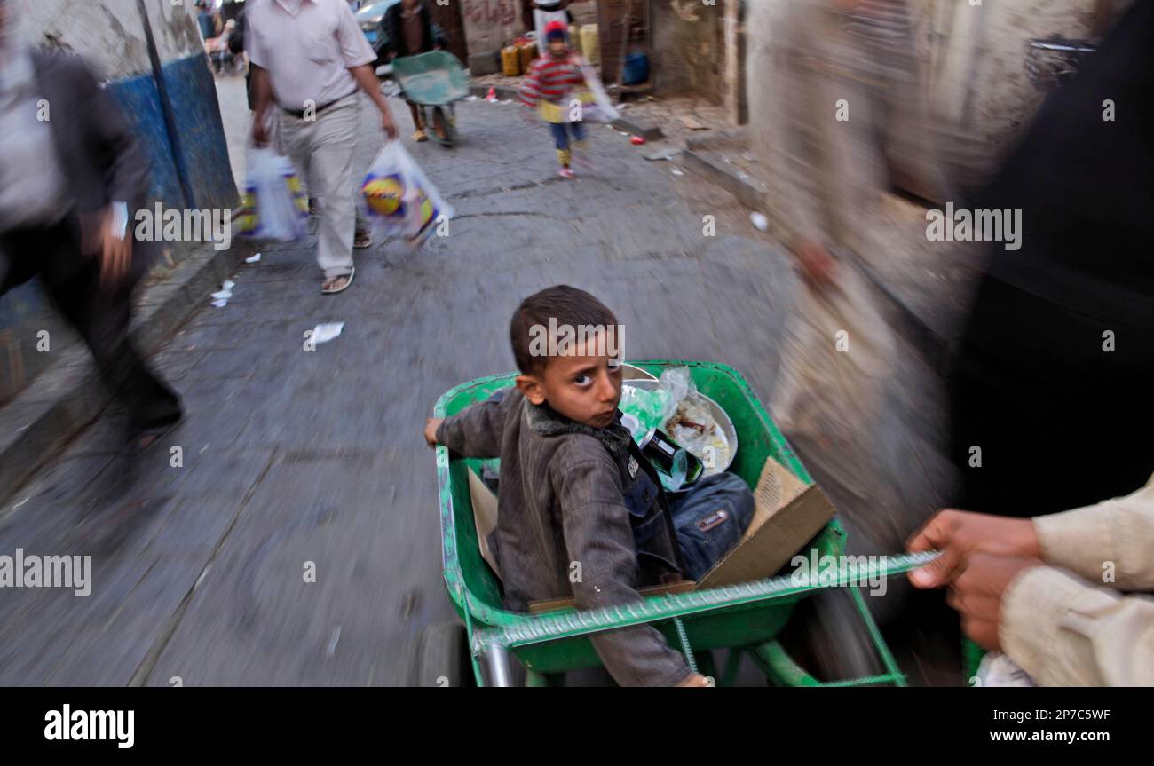 A Yemeni boy sitting on a cart looks back while being pushed by another ...