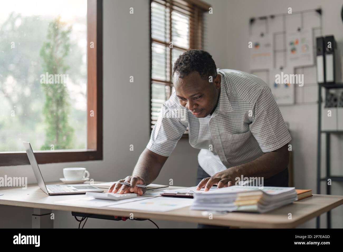 Happy African man using laptop computer and calculator for calculating ...