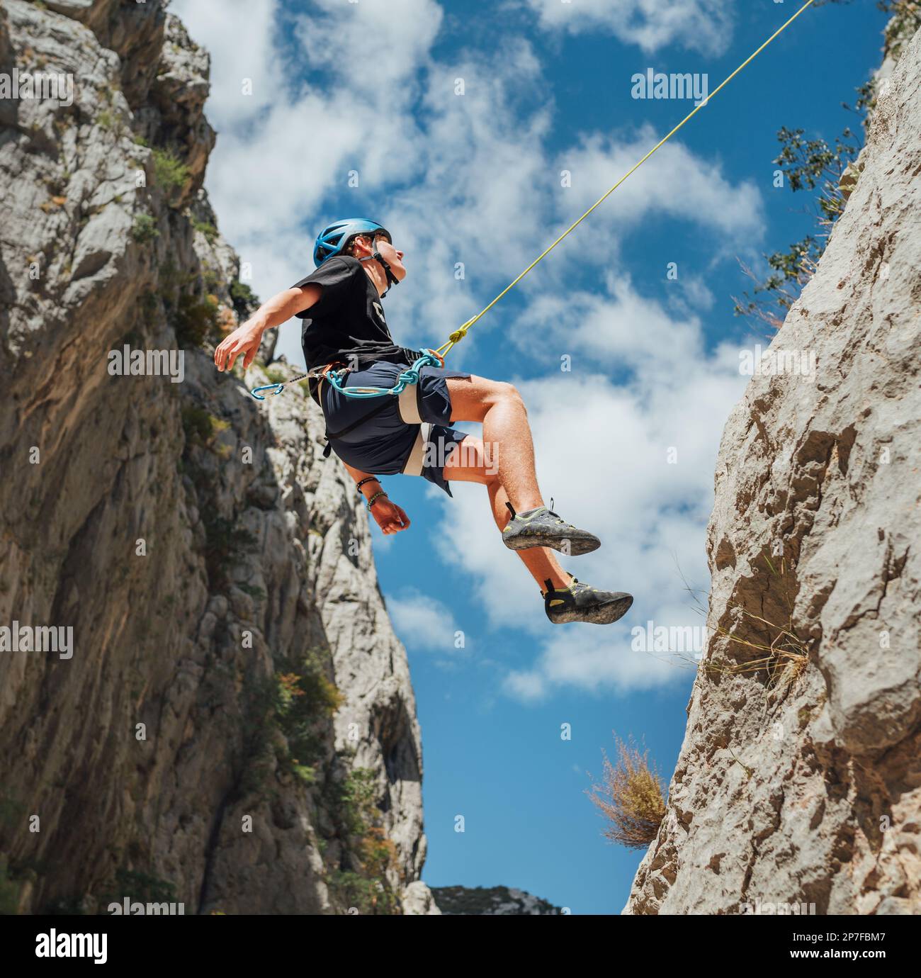 Climber teenage boy in protective helmet jumping on vertical cliff rock ...