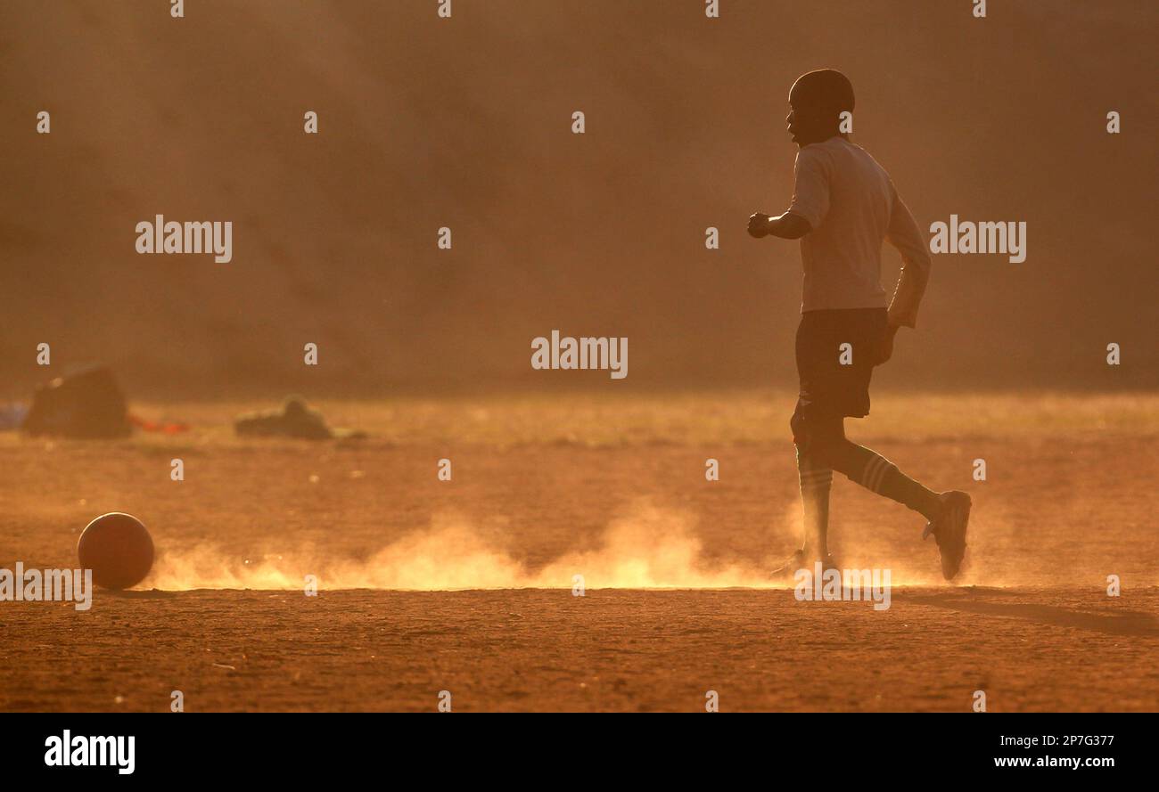 A boy plays soccer on a dusty pitch next to the New Zealand All Whites ...