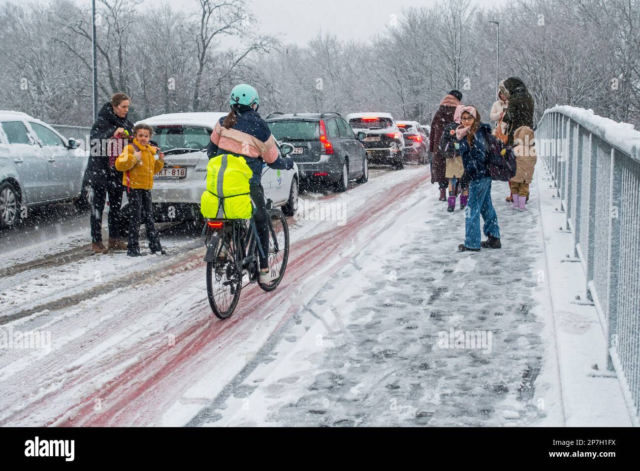 Cyclist and children walking to school over slippery pavement on bridge ...