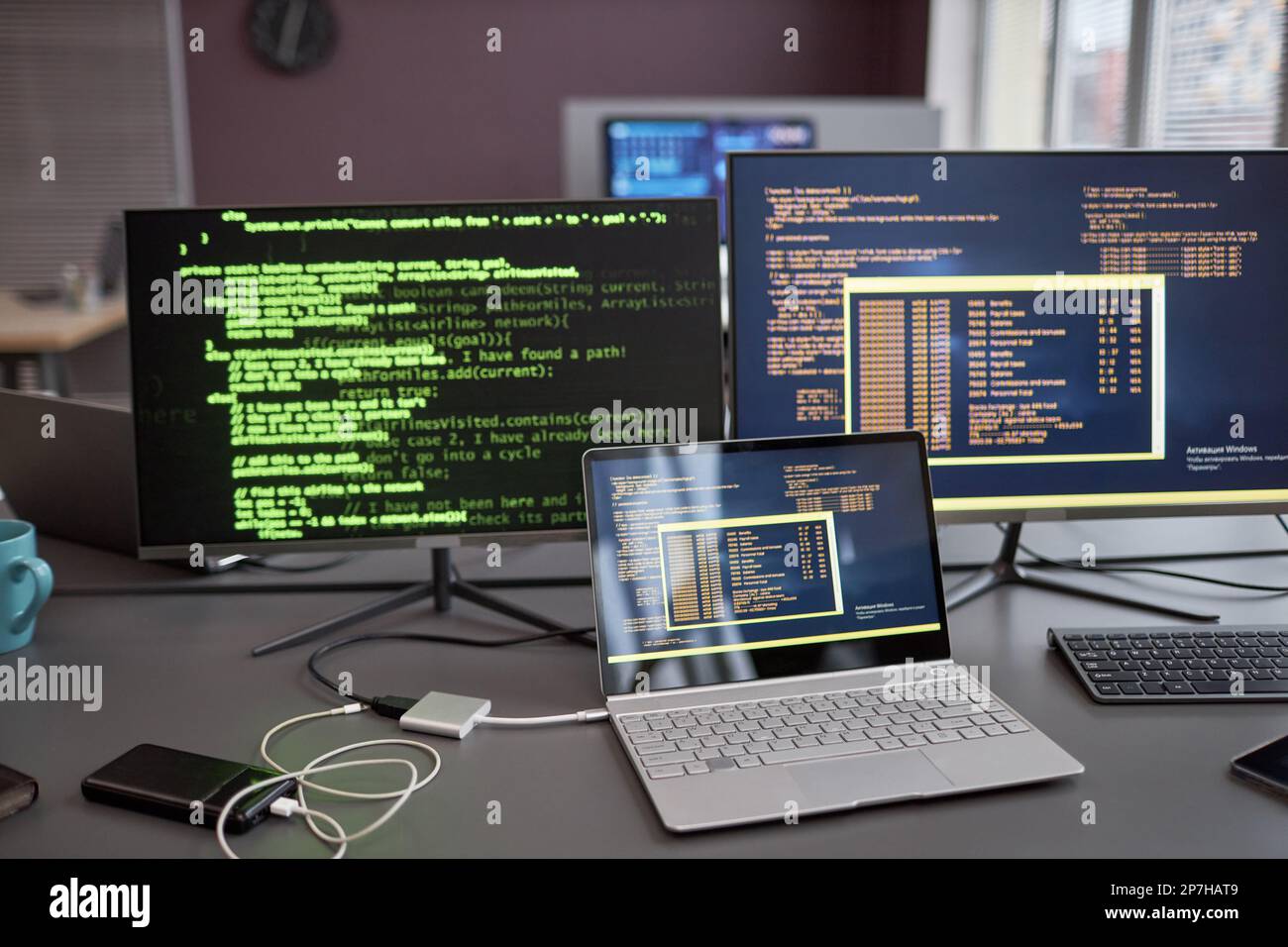 Background image of computers and laptops with green code lines on screen at workplace in IT ...