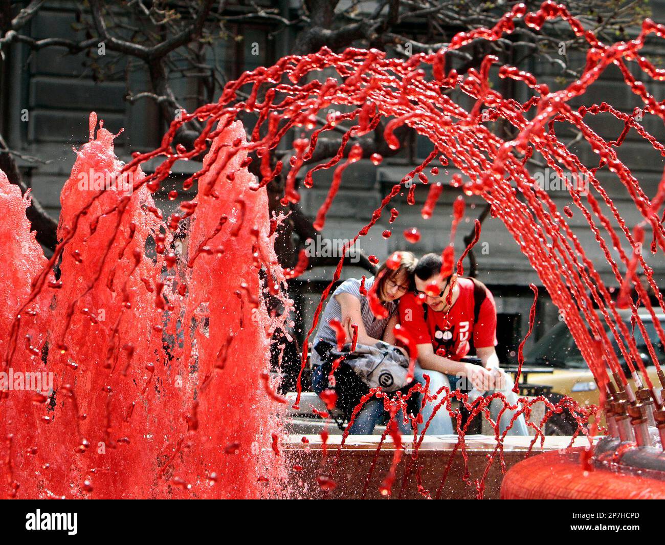 A couple sits on a bench seen through the red colored water of a ...