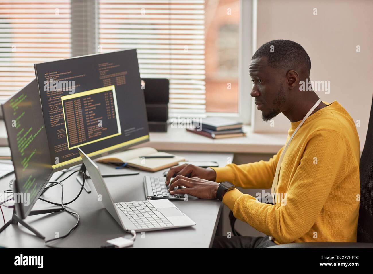 Side view portrait of young black man typing at keyboard and writing code in IT development ...