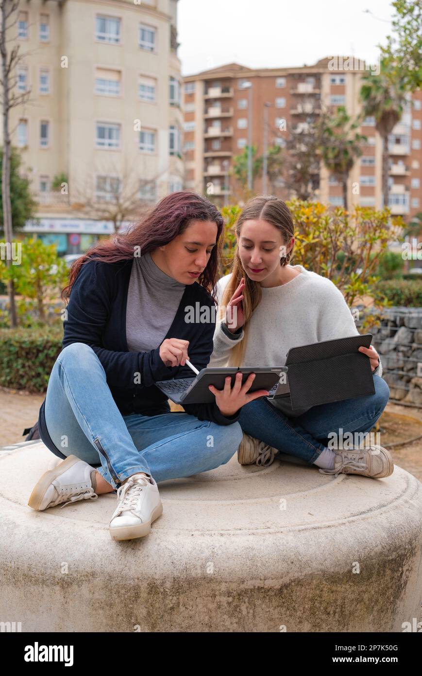 Two student friends talking and consulting notes on tablet abroad ...