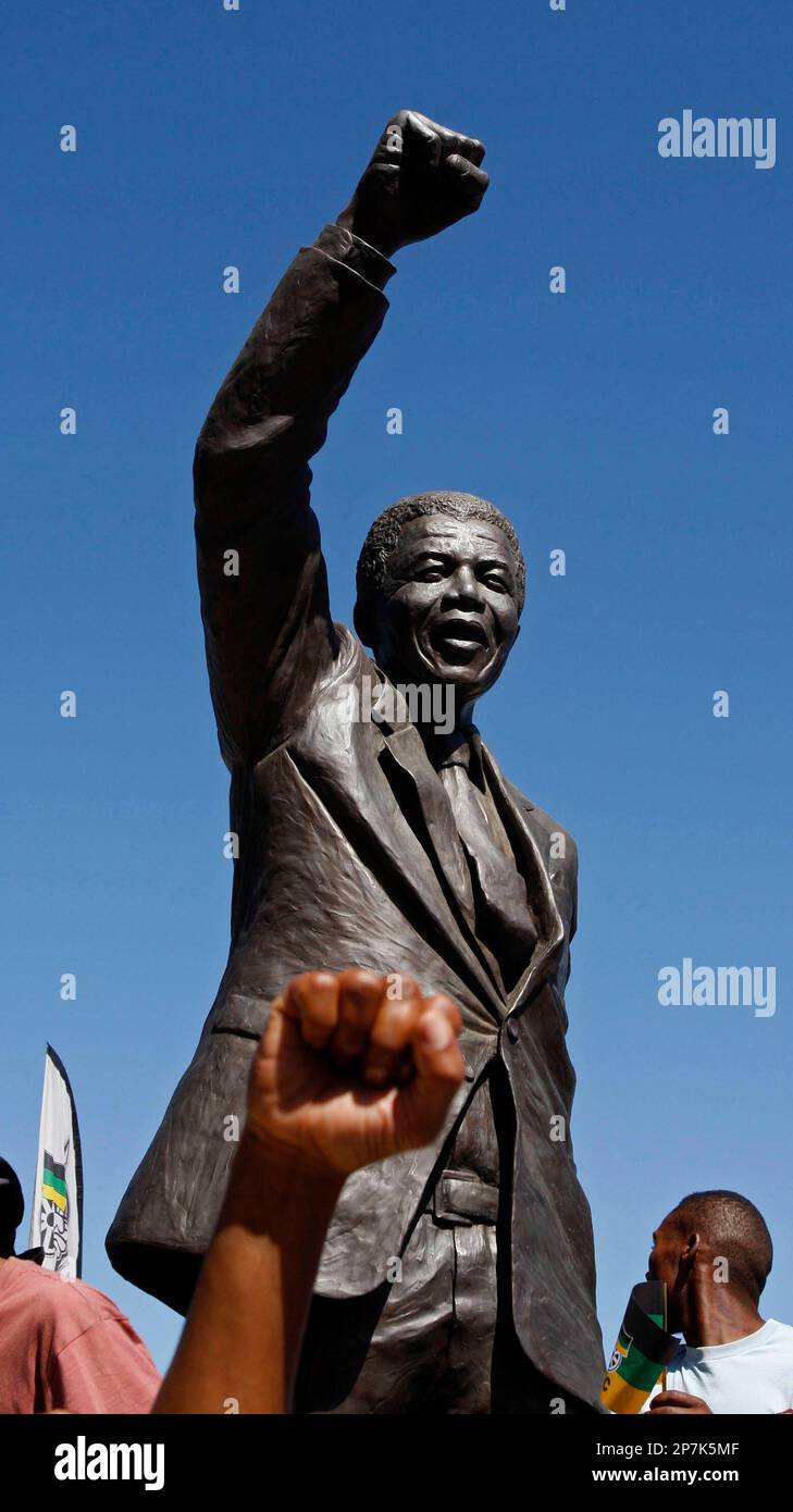 A man holds up his fist in front of the statue of former South African ...