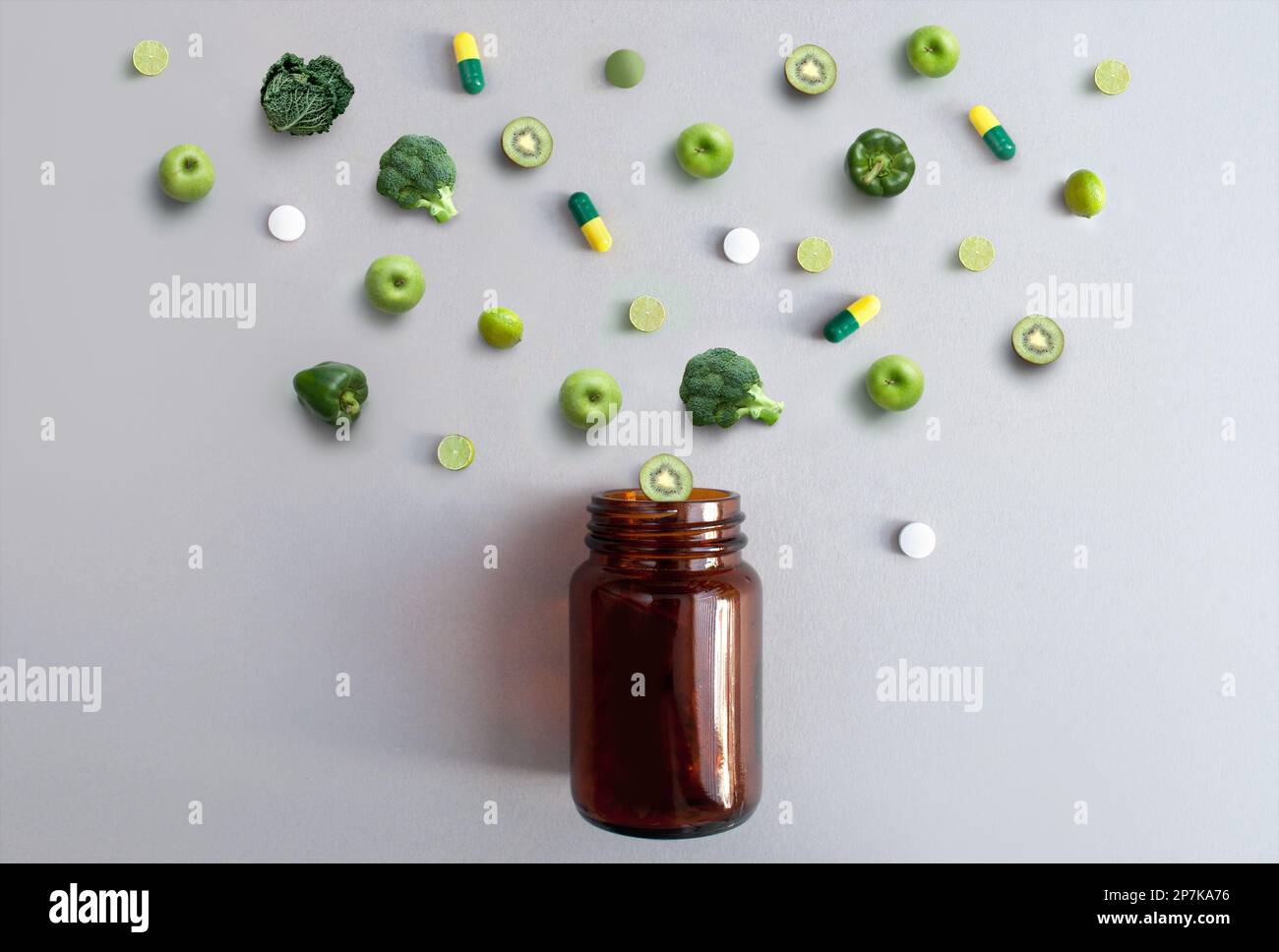 Green vitamin pills and capsules alongside apples, broccoli, cabbage ...
