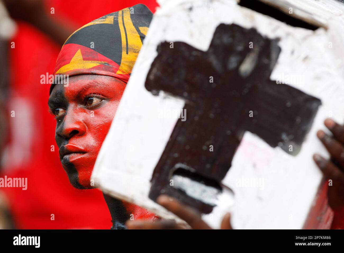 An Angola fan painted in the colors of Angola's flag carries a coffin ...