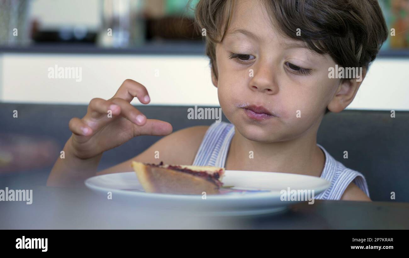 One small boy seated at breakfast table chewing food in front of bread ...