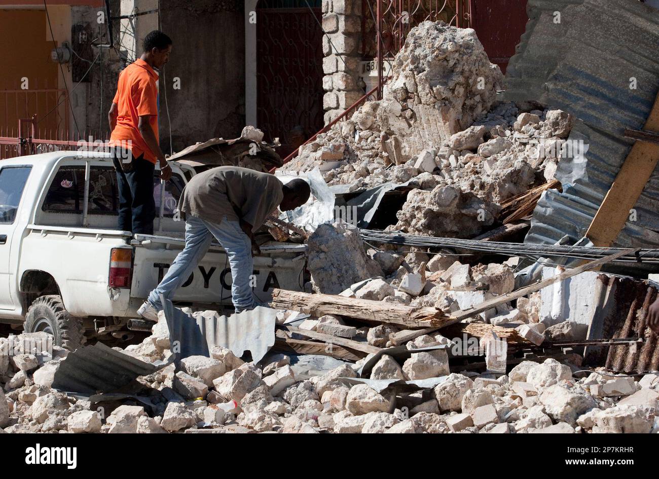 Two men clear debris from a car in the town of Jacmel, Haiti Monday ...