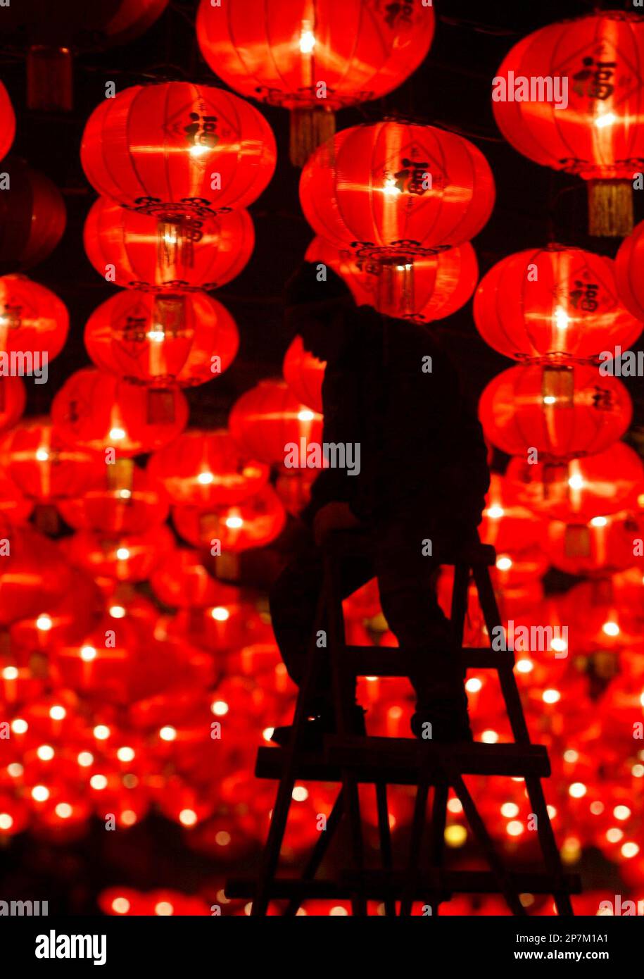 A worker is seen on a ladder while hanging red lanterns for a local festival in Shenyang, in ...