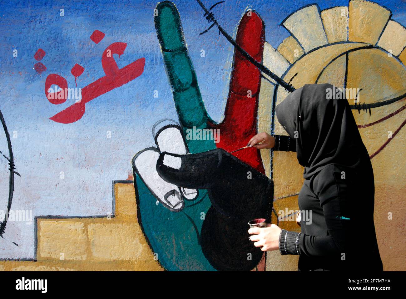 A young Palestinian woman paints a mural to commemorate the one-year ...
