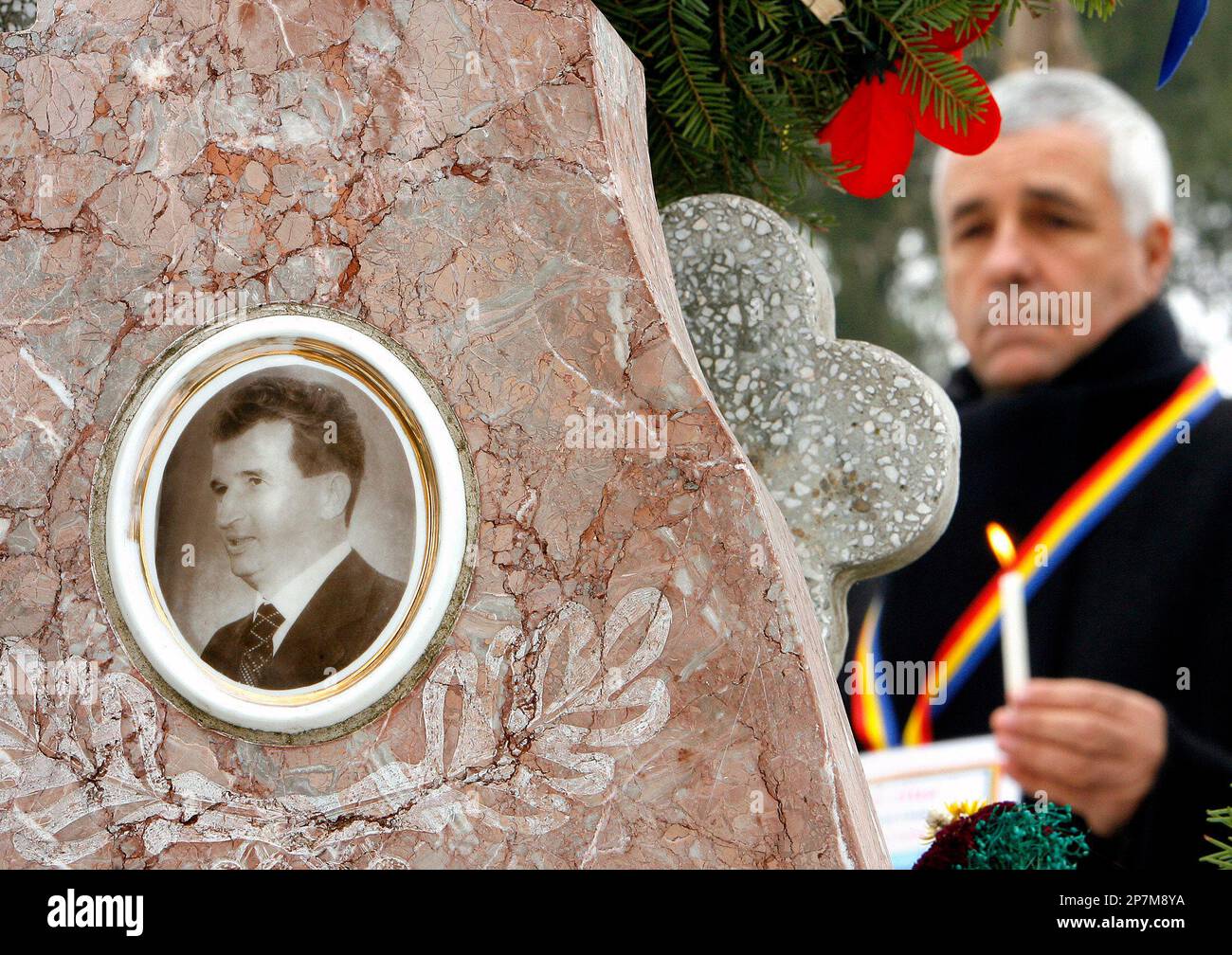 A man stands with a lit candle, next to the grave of late communist ...