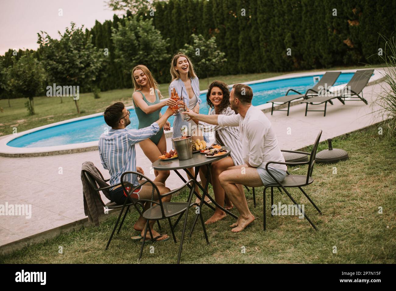 Group of happy young people cheering with cider by the pool in the ...