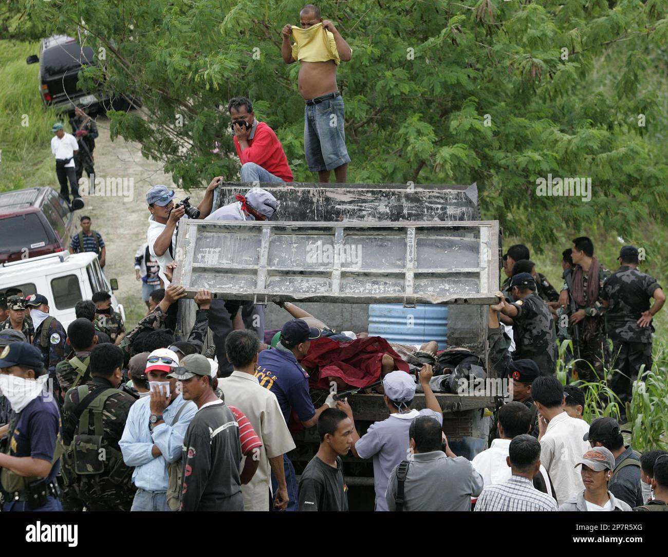 Civilians look on as police officers carry dead bodies on a dump truck ...