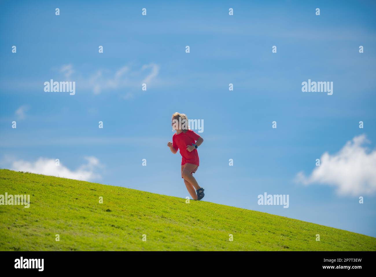Cute boy running across grass and summer sky. Sporty kid running in ...