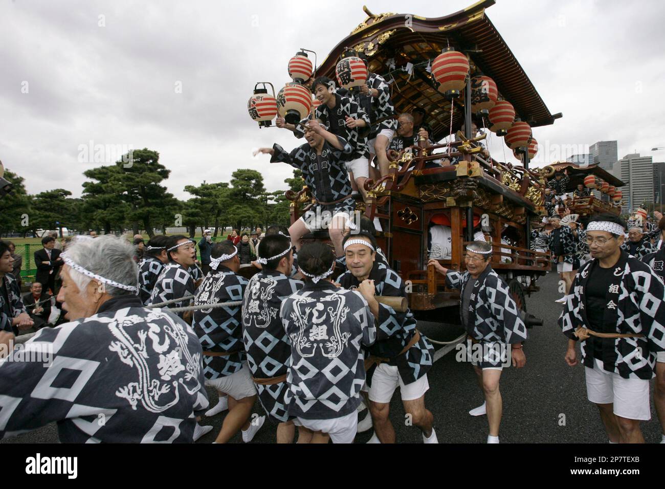 People in festival costume pull a float through a street in front of ...