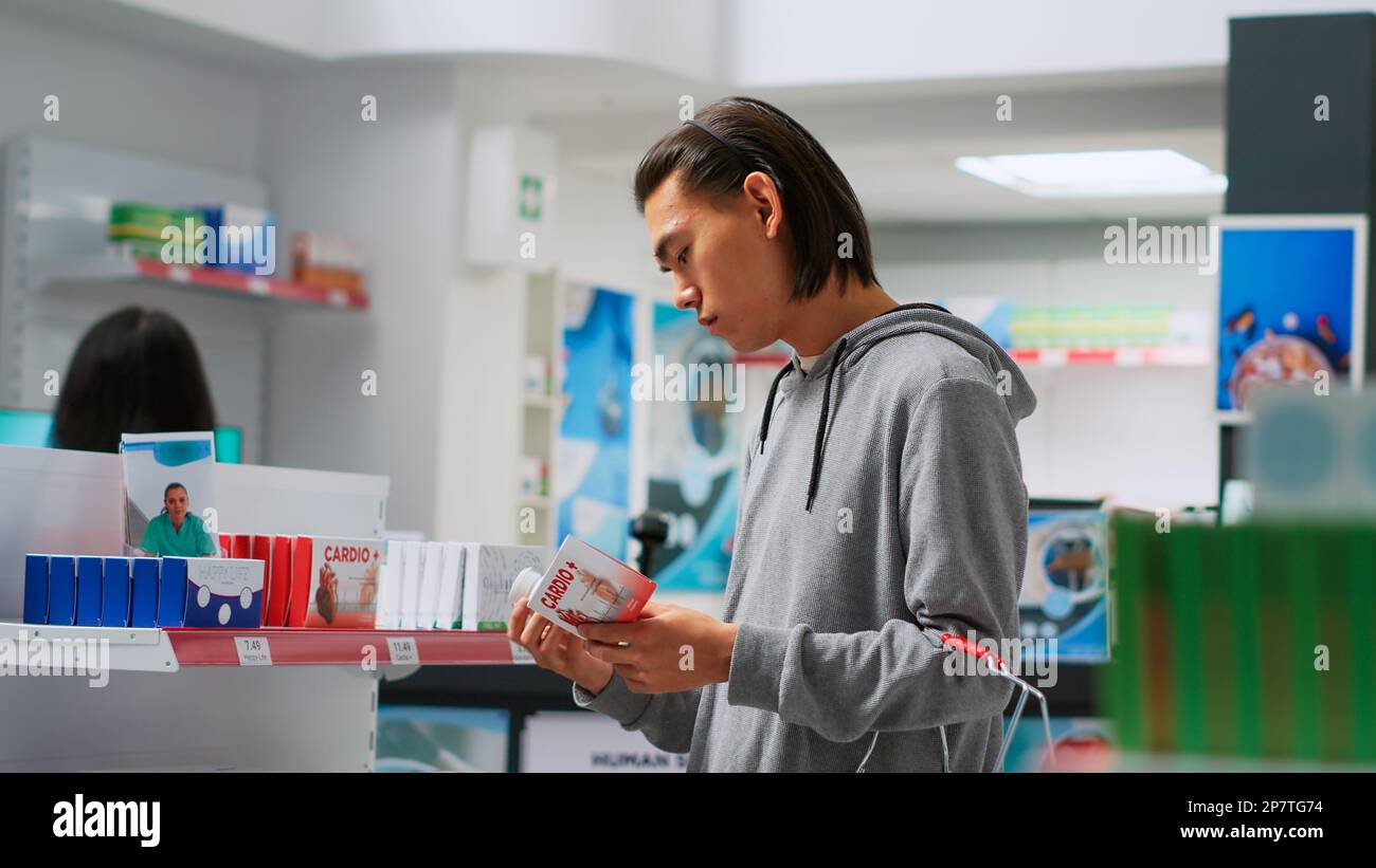Asian young man checking medical pills box in pharmacy, reading package ...