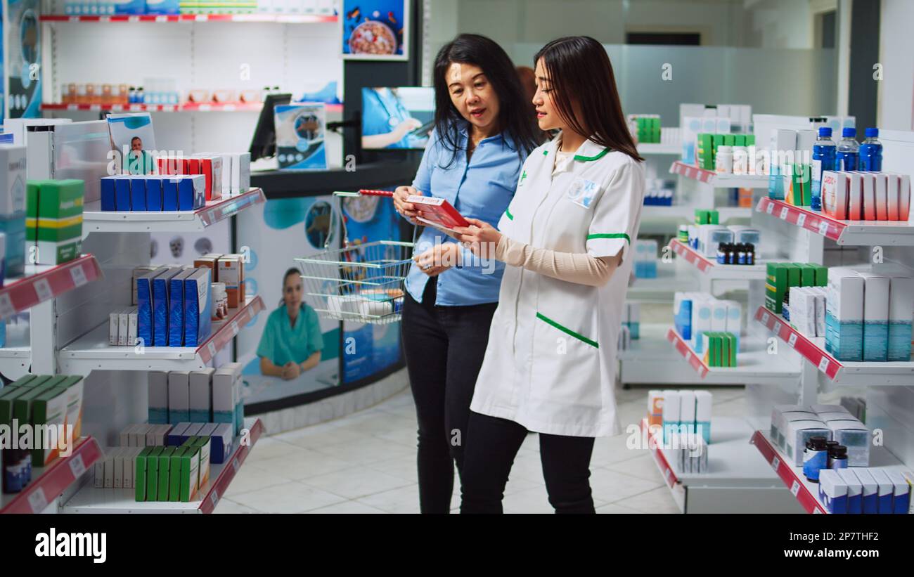 Young pharmacist giving support to woman in drugstore, reading ...