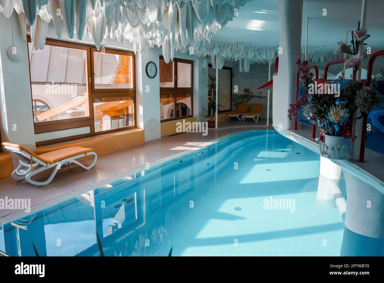 Empty lounge chair on tiled floor by window and swimming pool in hotel ...