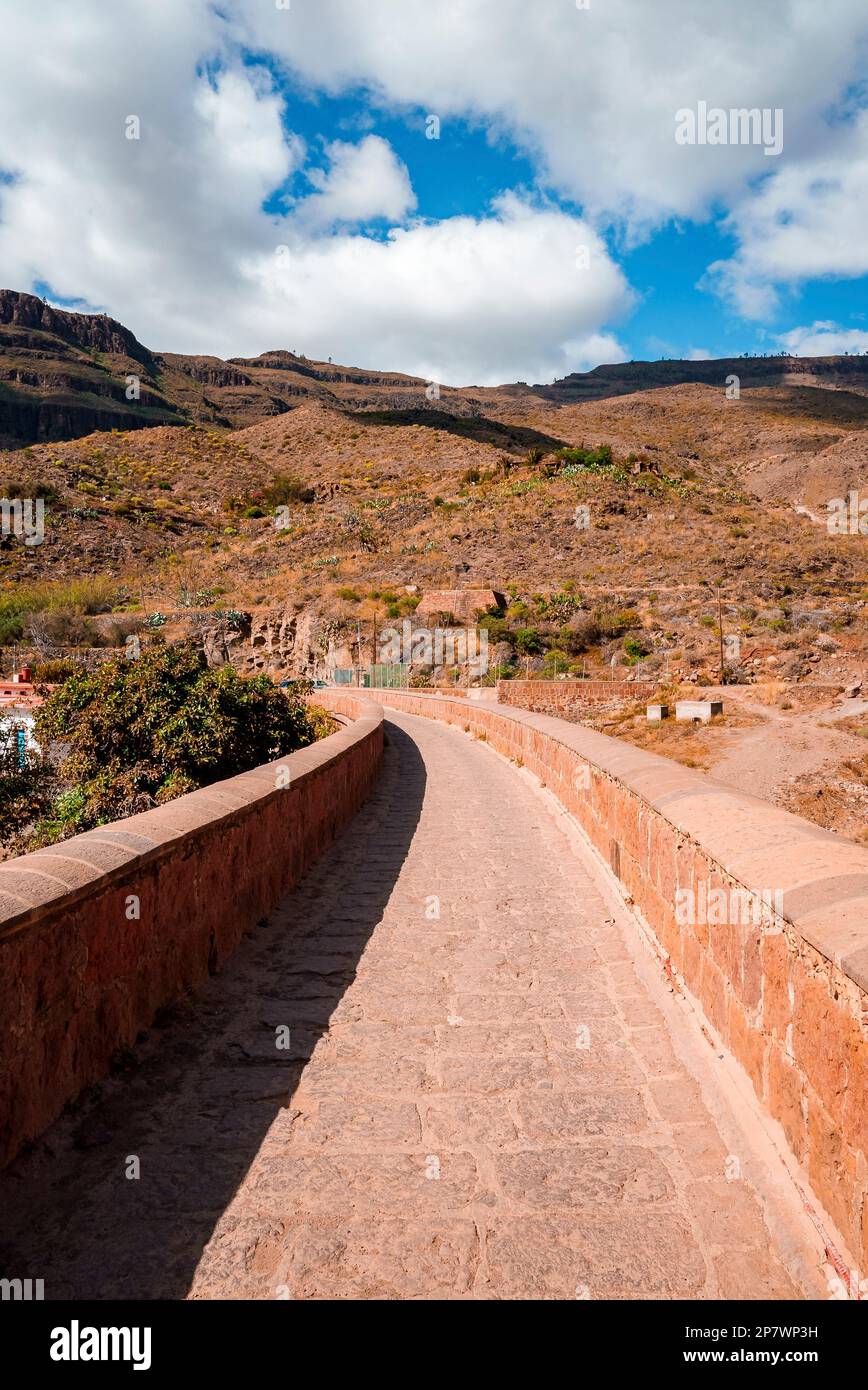 Footpath on dam leading towards rocky mountain landscape Stock Photo ...