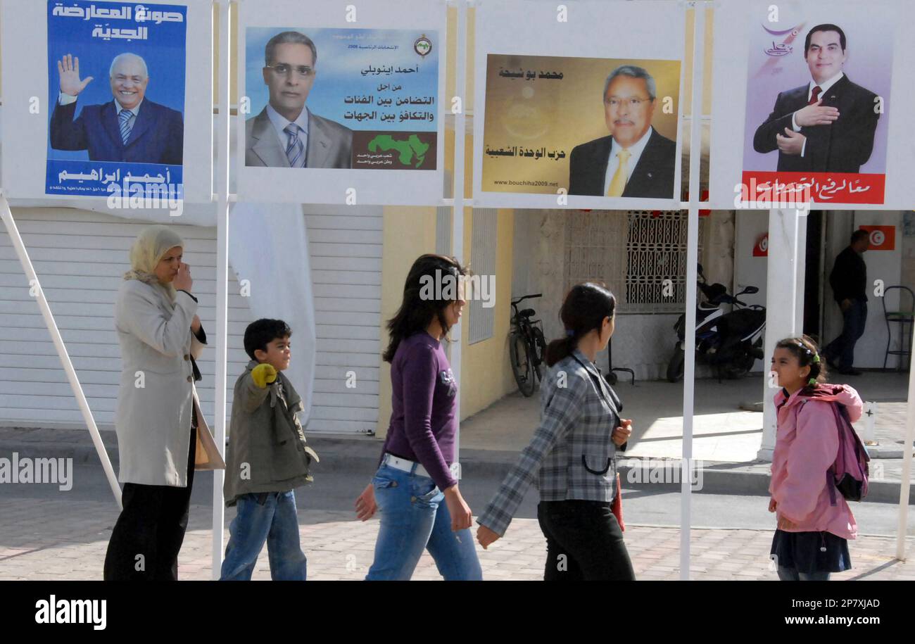 Tunisian walk past electoral posters of three officially approved ...
