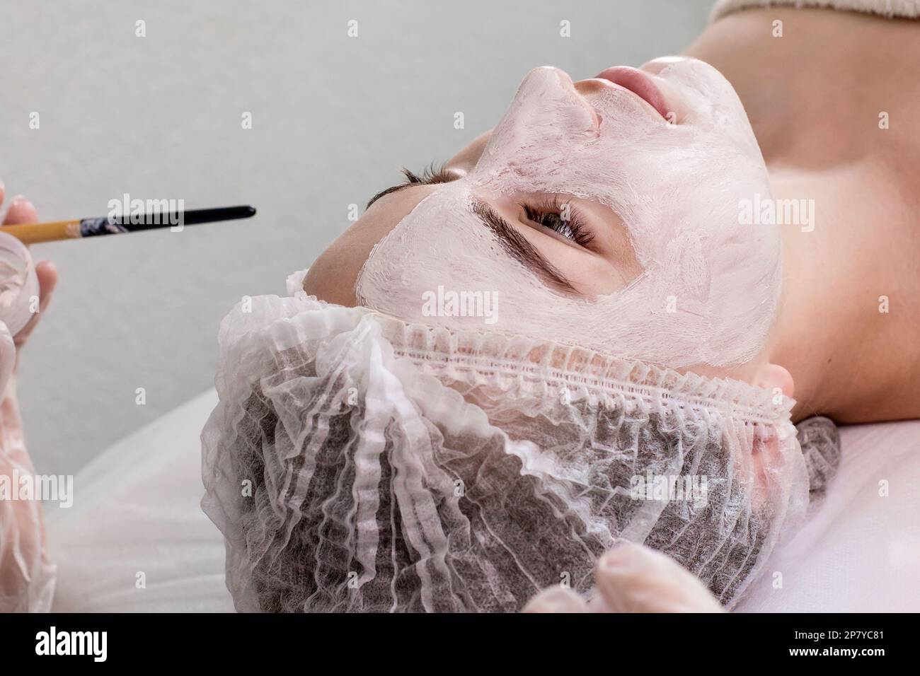A beautician applies a mask to the skin of a woman's face for ...