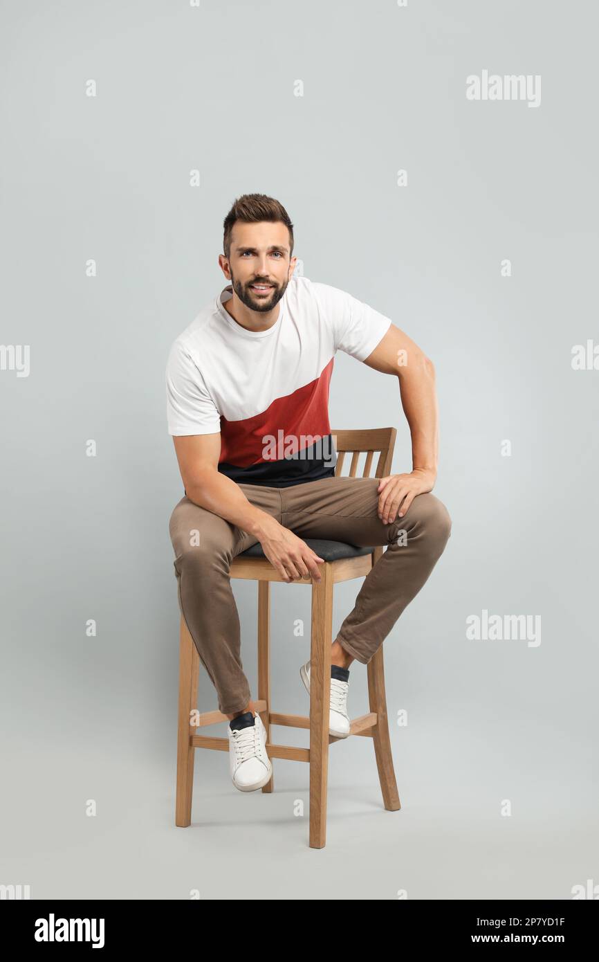 Handsome man sitting on stool against light grey background Stock Photo ...