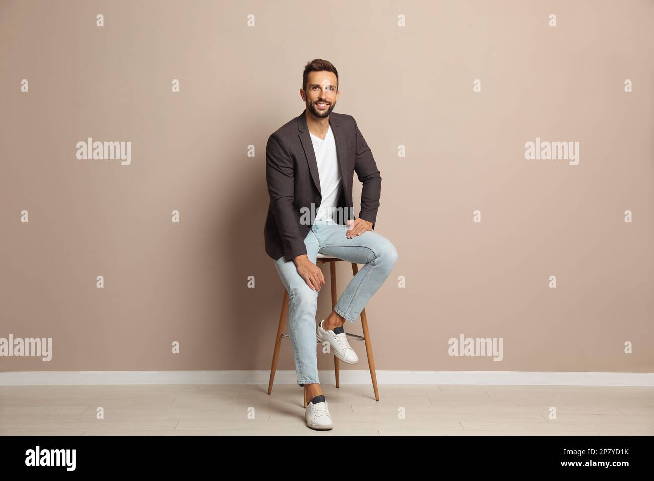 Handsome man sitting on stool near beige wall Stock Photo - Alamy