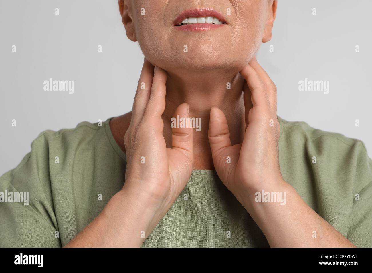 Mature woman doing thyroid self examination on light grey background ...