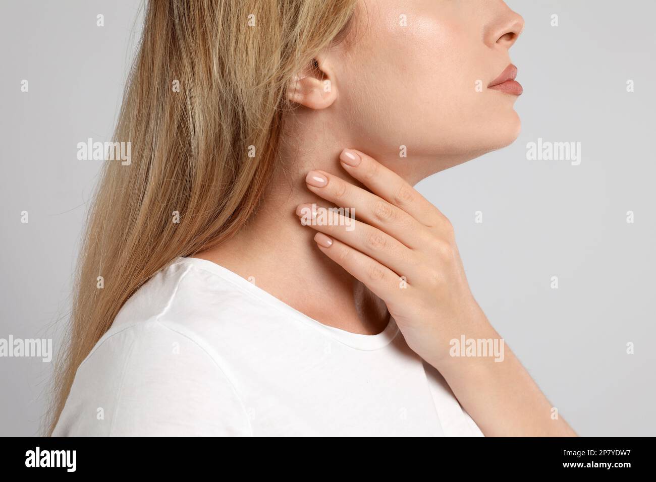 Young woman doing thyroid self examination on light grey background ...