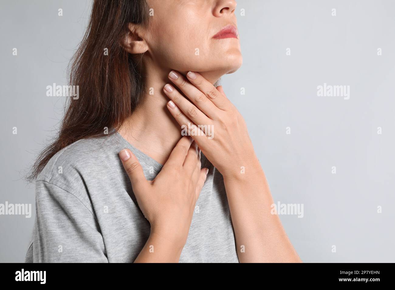 Mature woman doing thyroid self examination on light background ...