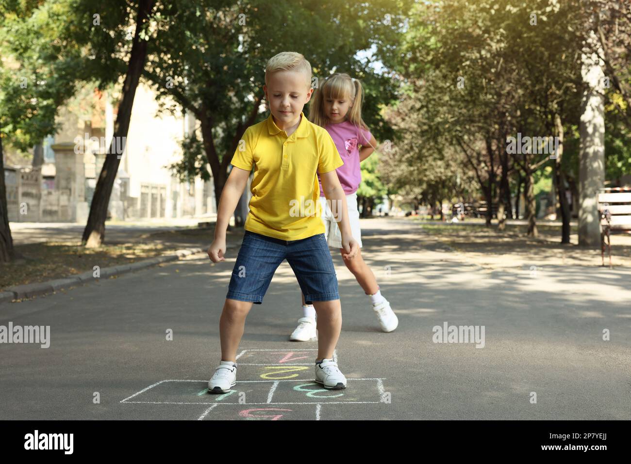 Little children playing hopscotch drawn with chalk on asphalt outdoors ...