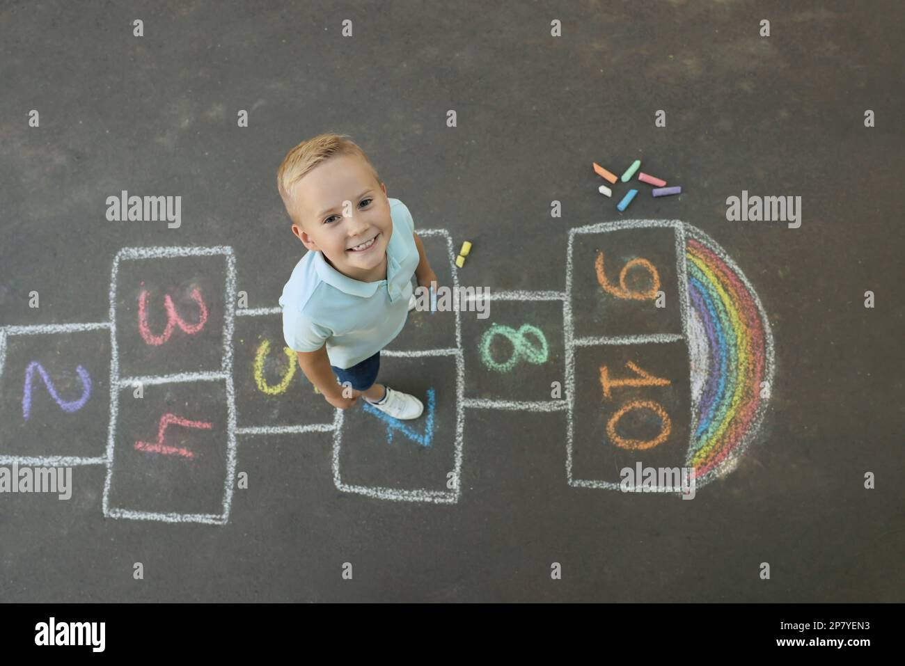 Little boy and colorful hopscotch drawn with chalk on asphalt outdoors ...