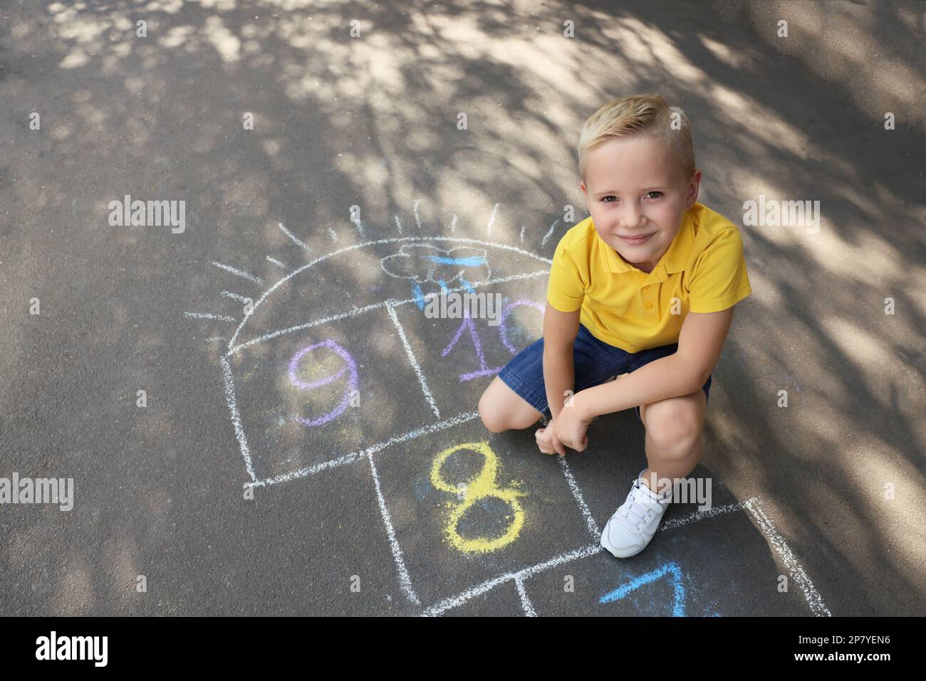 Little boy drawing hopscotch with chalk on asphalt outdoors. Happy ...