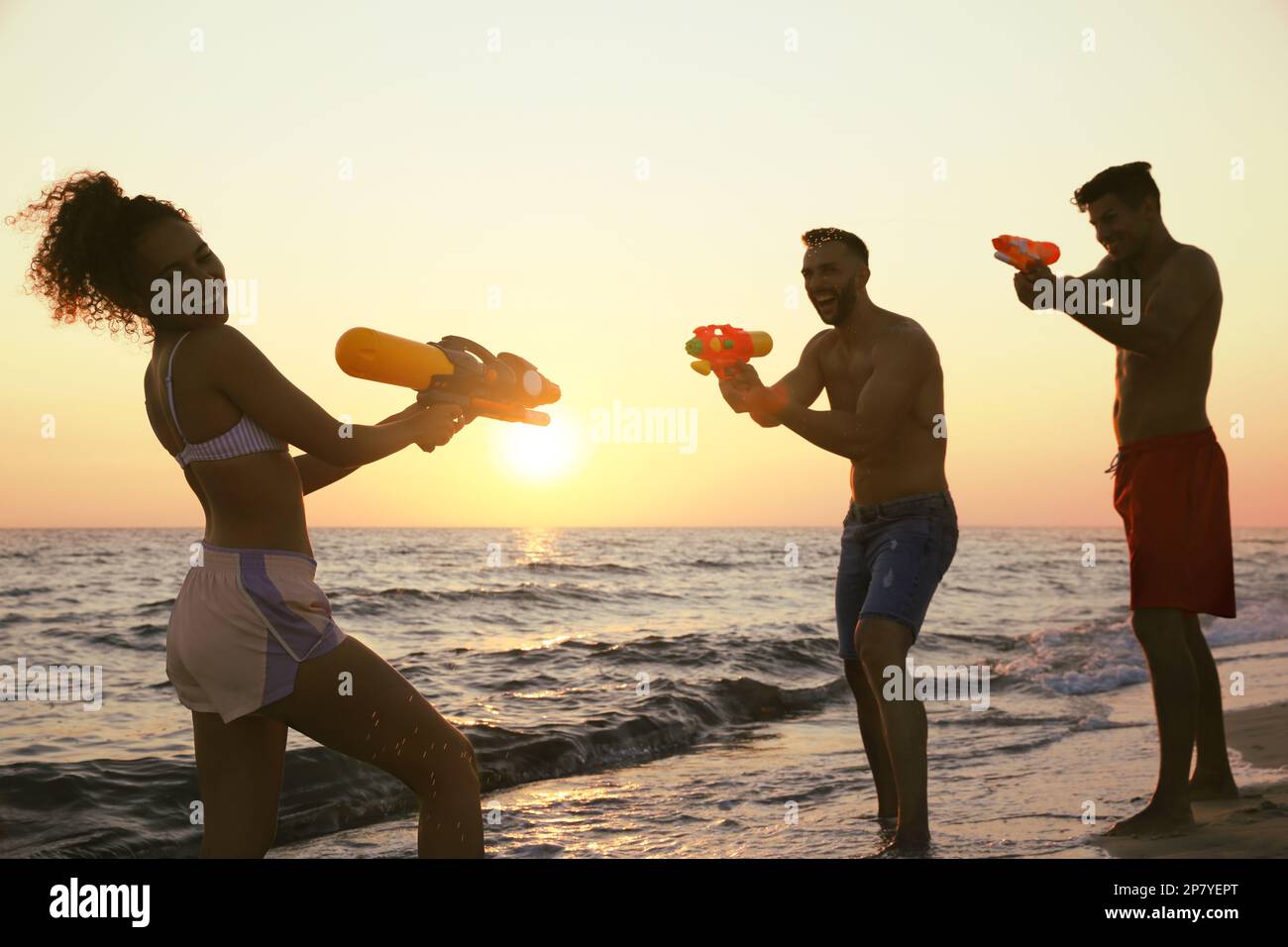 Friends with water guns having fun on beach at sunset Stock Photo - Alamy