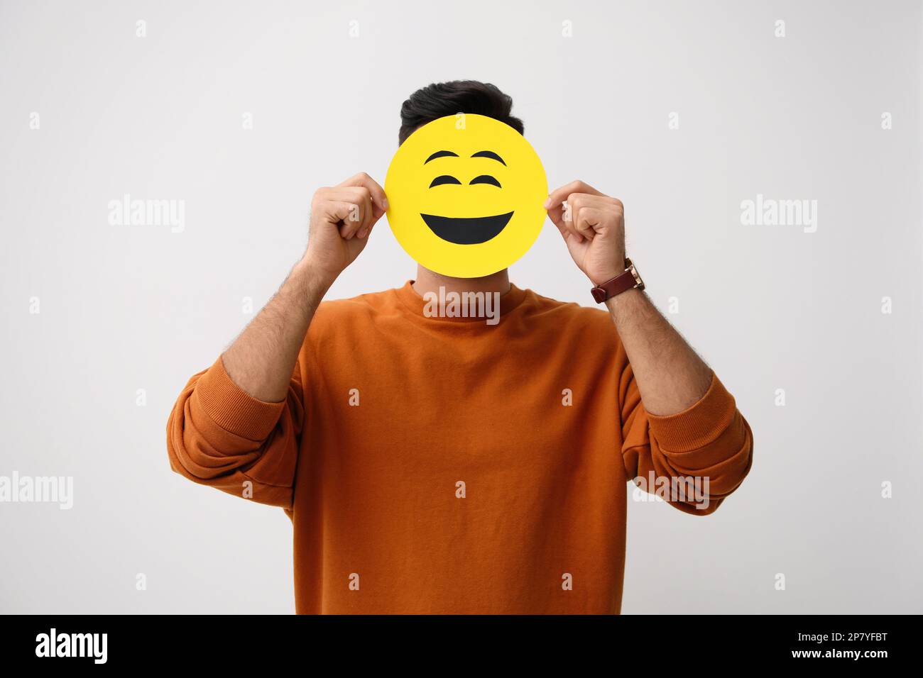Man hiding emotions using card with drawn smiling face on white ...