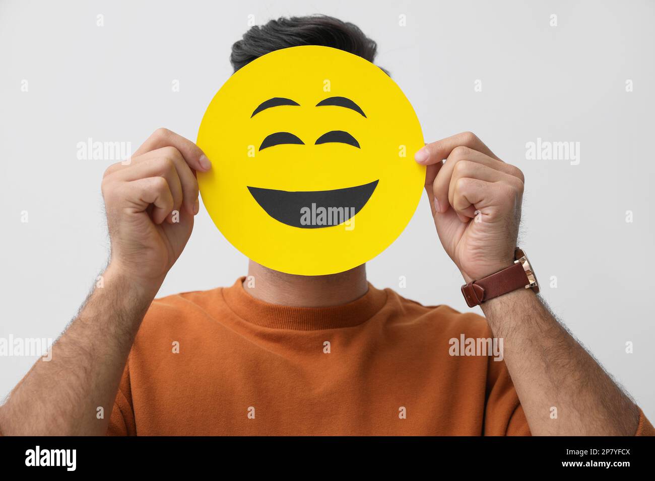 Man hiding emotions using card with drawn smiling face on white ...