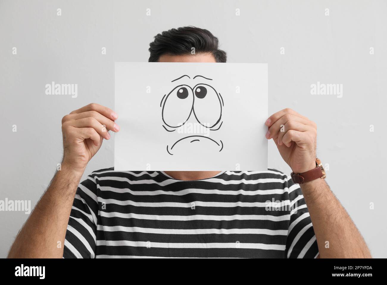 Man hiding emotions using card with drawn frowning face on white ...