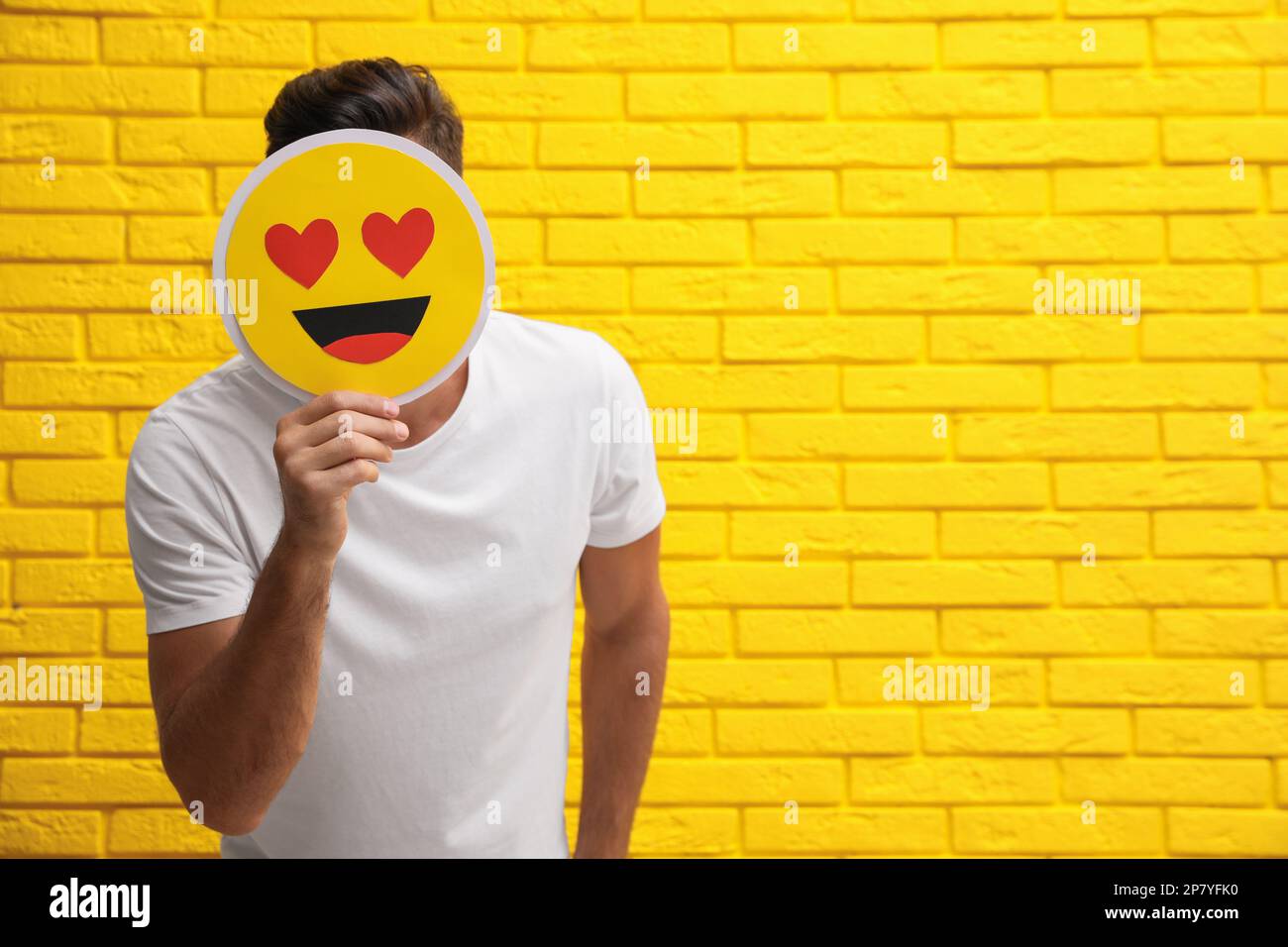 Man hiding emotions using card with drawn smiling face near yellow ...