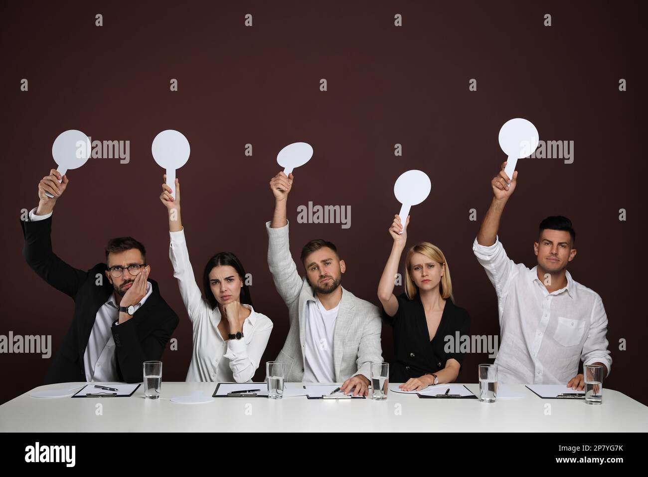Panel of disappointed judges holding blank score signs at table on ...