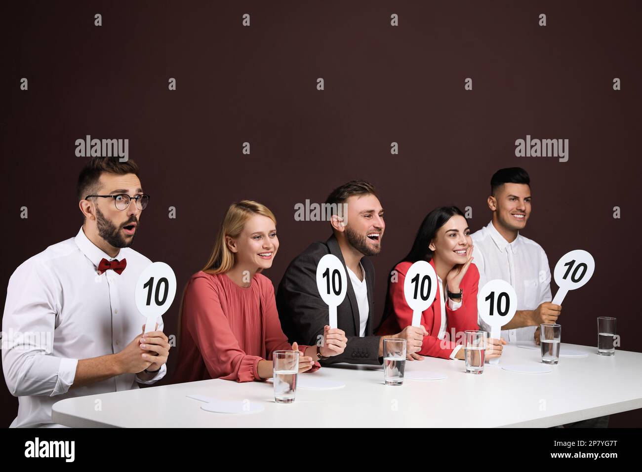 Panel of judges holding signs with highest score at table on brown ...