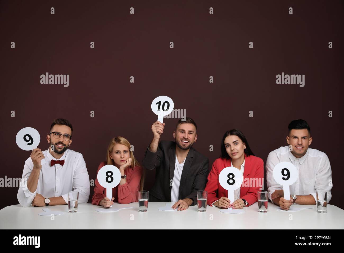 Panel of judges holding different score signs at table on brown ...