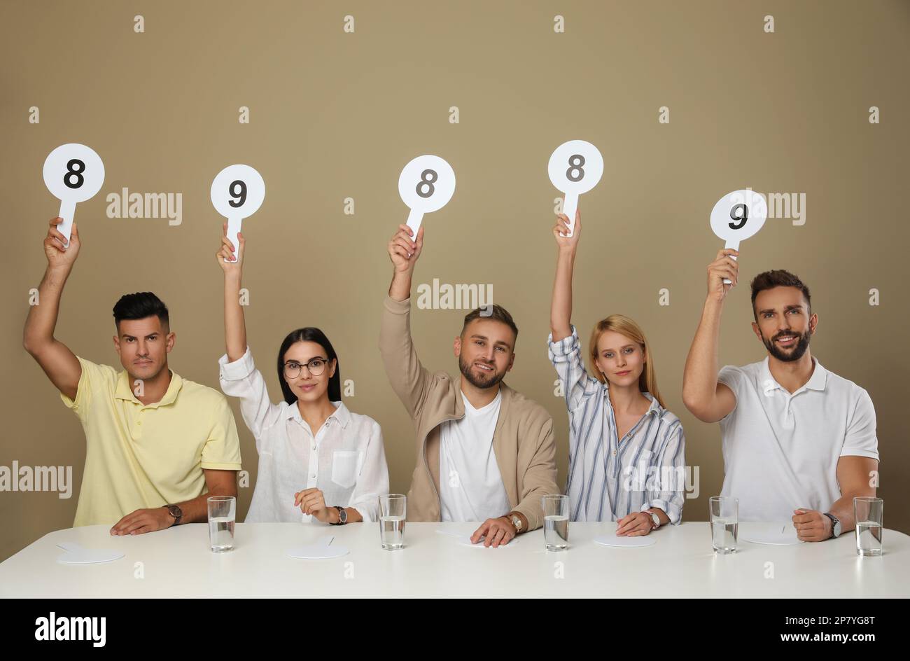 Panel of judges holding different score signs at table on beige ...