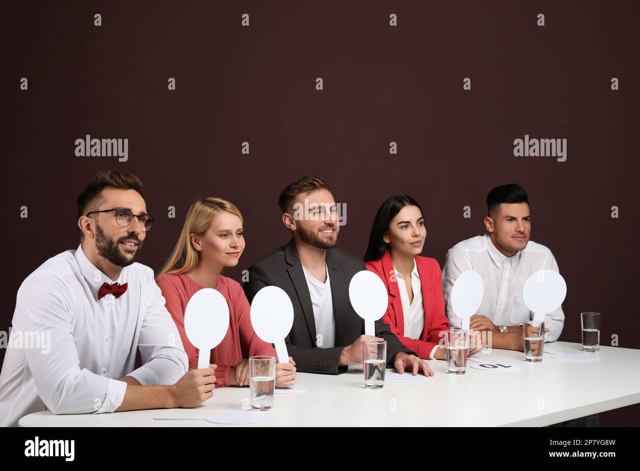 Panel of judges holding blank score signs at table on brown background ...