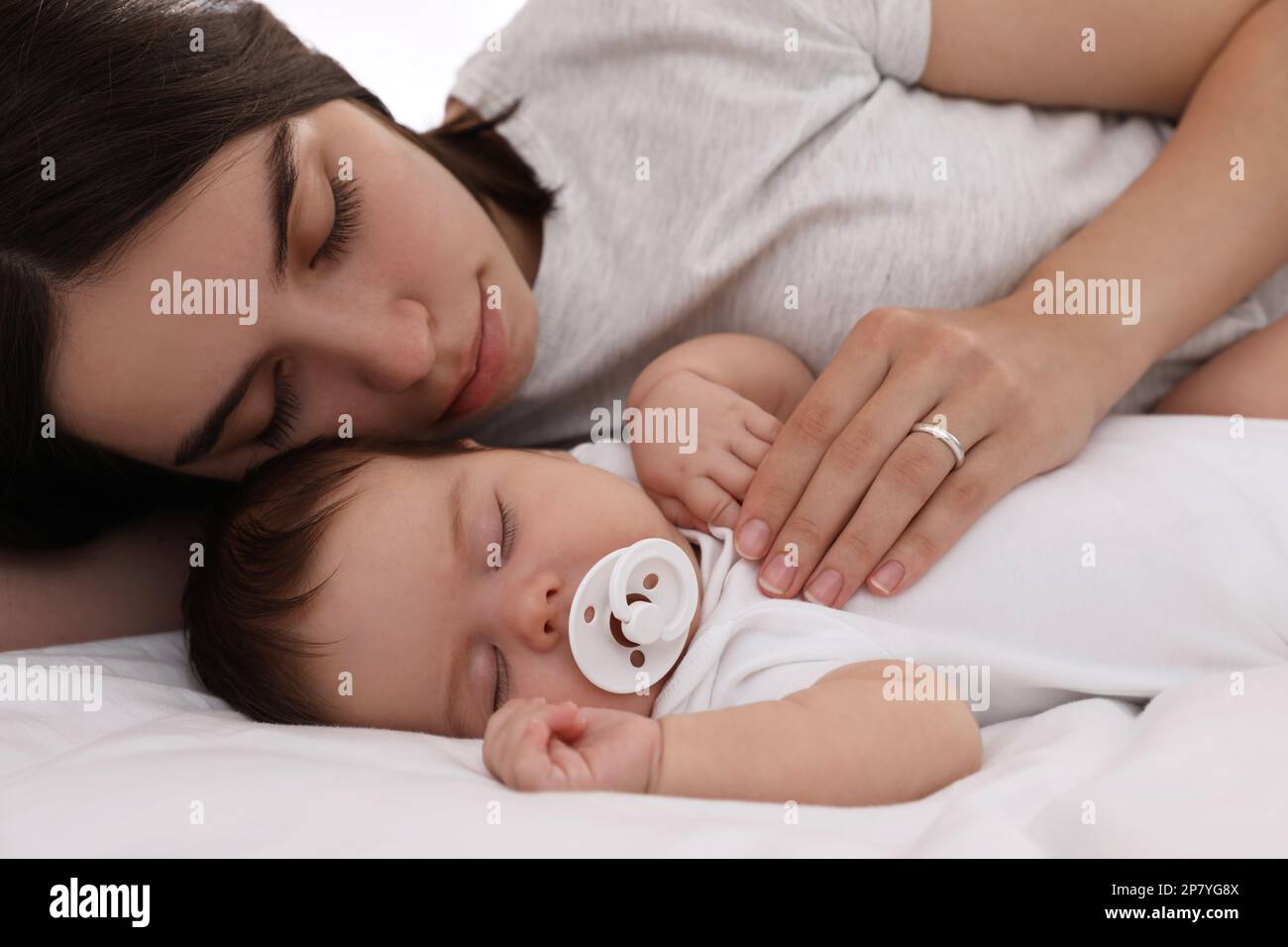 Young mother resting near her sleeping baby on bed, closeup Stock Photo ...